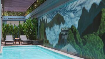 Piscina com um mural de montanhas e área coberta com espreguiçadeiras e uma mesa.
