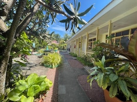 Caminho que leva a um edifício com galeria coberta e vasos de plantas.
