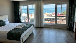 Quarto de hotel com uma grande janela que oferece vista para o mar e para a paisagem urbana.