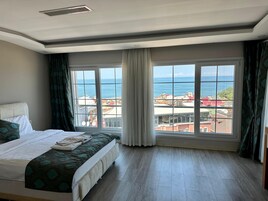 Quarto de hotel com uma grande janela que oferece vista para o mar e para a paisagem urbana.