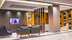 Um lobby moderno com áreas de estar, uma tela de televisão e uma parede decorativa com elementos verticais.