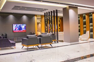 Um lobby moderno com áreas de estar, uma tela de televisão e uma parede decorativa com elementos verticais.