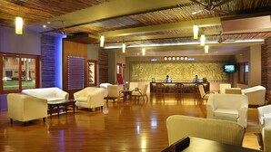 Um saguão de hotel com balcão de recepção, área de estar e uma grande decoração na parede.