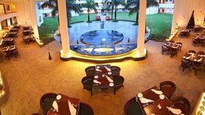 Um saguão de hotel com várias áreas de refeições, uma fonte central e vista para o jardim exterior.