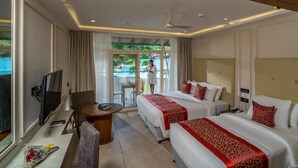 Quarto de hotel com duas camas, televisão, escrivaninha e vista para uma piscina ao ar livre.