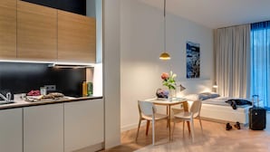 Quarto de hotel moderno com cozinha compacta, área de refeições, cama e vista para o exterior.