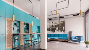 Um interior moderno com cozinha em tons de verde-água, um bar com banquetas e uma área de estar com sofá azul e um grande mural na parede.