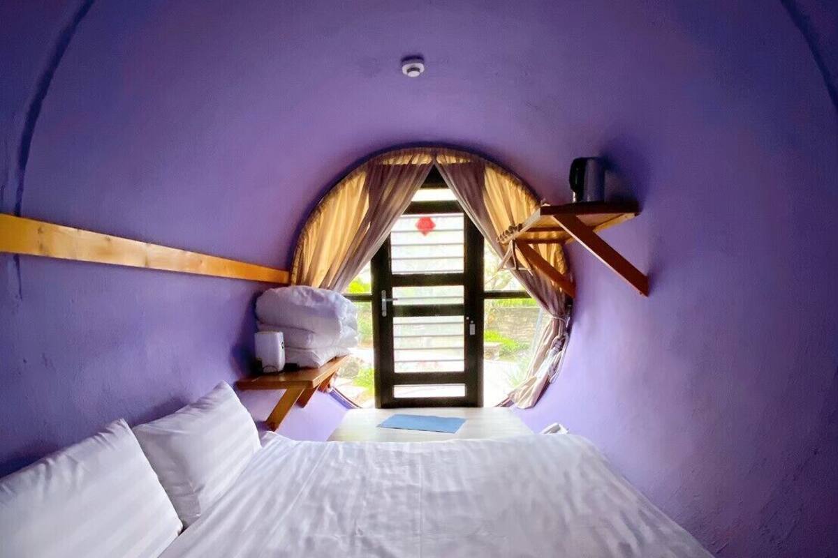 Quarto com cama, janela com cortinas e pequena mesa com abajur.