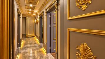 Corredor com detalhes dourados elaborados, piso de mármore e portas que dão acesso a quartos.