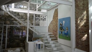 Um interior moderno com escada de vidro, parede de tijolos e obras de arte nas paredes.