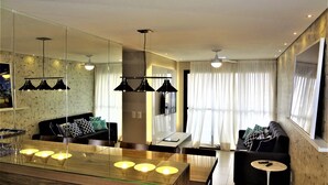 Uma sala de estar moderna com uma mesa de jantar de vidro, sofás pretos e um espelho grande.