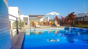 Uma piscina com cadeiras de descanso e guarda-sóis, cercada por edifícios.