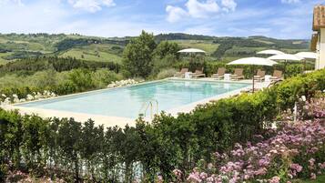 Piscina retangular com superfície de água azul cristalina, rodeada por vegetação exuberante e flores cor-de-rosa.