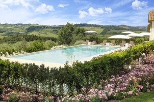 Piscina retangular com superfície de água azul cristalina, rodeada por vegetação exuberante e flores cor-de-rosa.