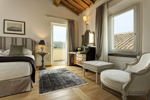 Quarto com cama, poltrona, cômoda, espelho, abajur e vista para o exterior.
