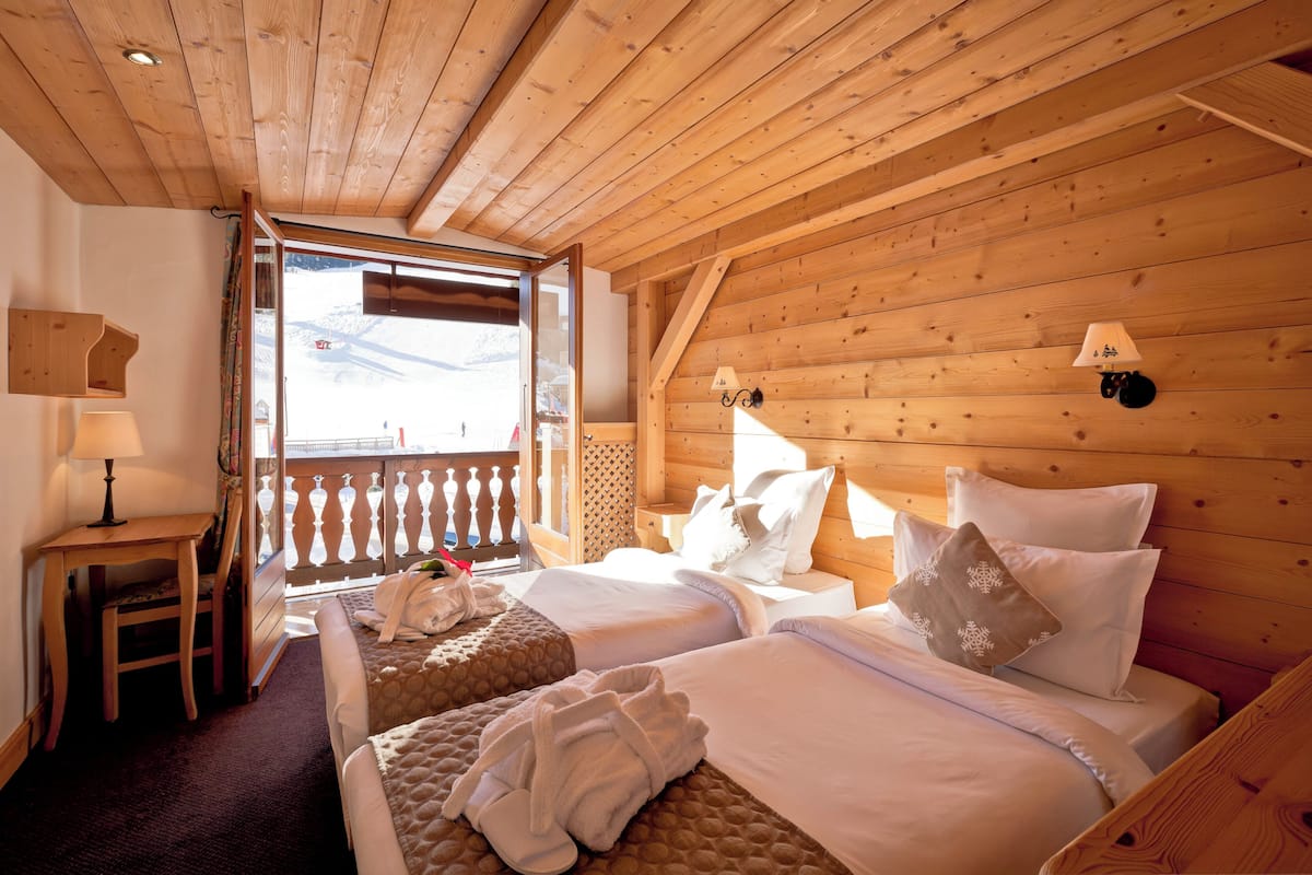 Quarto de cabana de madeira com duas camas, uma escrivaninha e janela com vista para uma paisagem coberta de neve.