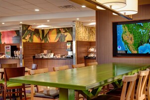Restaurante com uma longa mesa verde, cadeiras de madeira e uma tela grande exibindo um mapa.