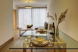 Uma sala de jantar com uma mesa de vidro posta para dois, com um bowl, pratos, talheres e copos.