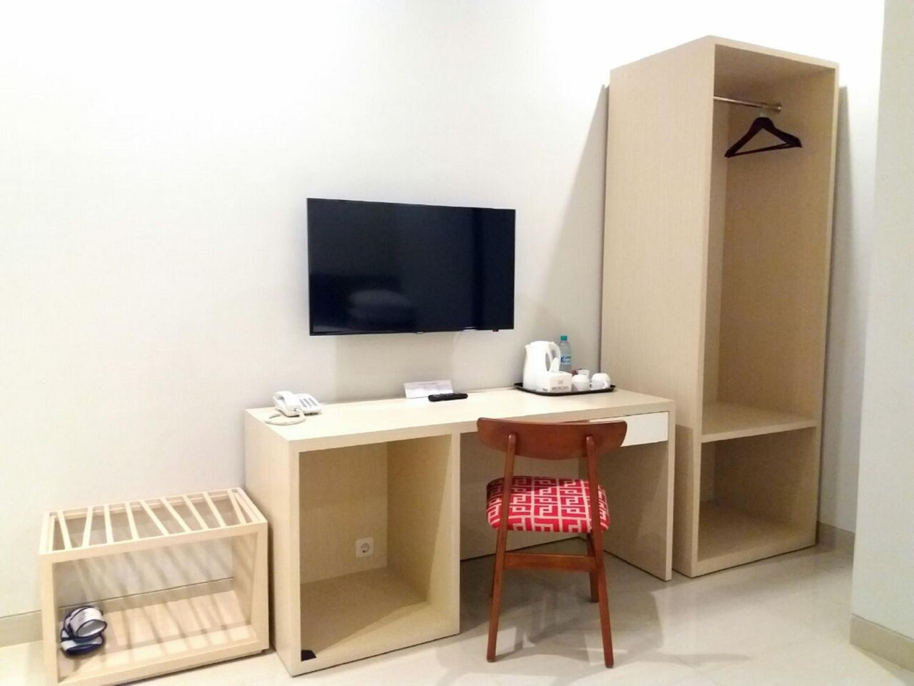 Quarto pequeno e moderno com escrivaninha, cadeira, televisão e guarda-roupa.