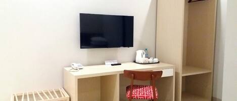 Quarto pequeno e moderno com escrivaninha, cadeira, televisão e guarda-roupa.