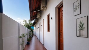 Corredor com plantas em vasos, piso de azulejos e porta de madeira.