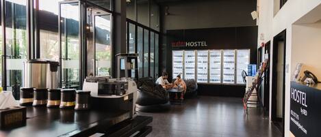 Interior moderno de um hostel, com espaço para café, áreas de estar e uma grande janela com vista.