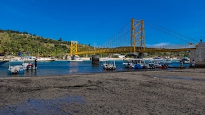Uma área costeira com uma ponte amarela, barcos e uma praia de areia.