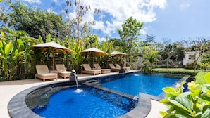 Piscina com espreguiçadeiras e guarda-sóis, rodeada por vegetação exuberante.