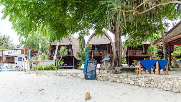 Um resort à beira-mar com bangalôs de telhado de palha, uma praia de areia e uma placa com informações.