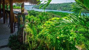 Construção com telhado de palha, com vista para um corpo d'água e vegetação exuberante.
