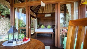 Um quarto de madeira com uma cama, uma mesa com um candeeiro e uma parede de pedra lá fora.