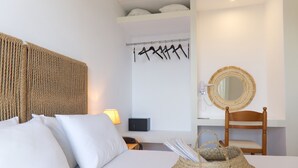 Quarto de hotel bem arrumado com cama, abajur, espelho fixado na parede, cadeira de madeira e cesta de palha na cama.