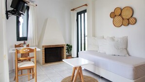 Uma sala de estar com um sofá branco, uma mesa pequena, uma cadeira de madeira, uma lareira e uma TV fixada na parede.