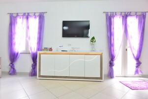 Uma sala de estar moderna com um rack branco, uma televisão de tela plana montada acima e cortinas roxas.