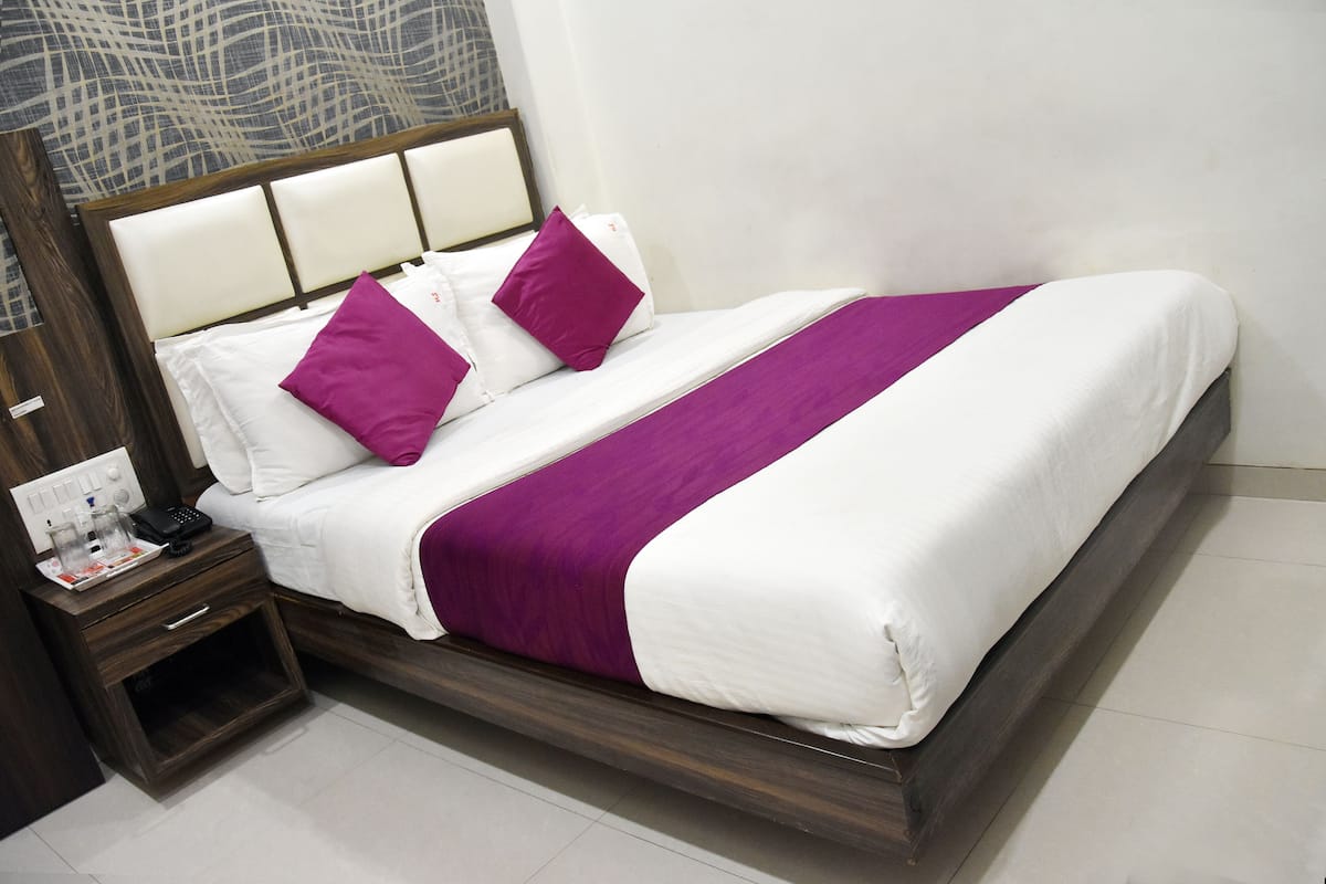 Uma cama bem arrumada com cabeceira de madeira, roupa de cama branca e duas almofadas roxas.