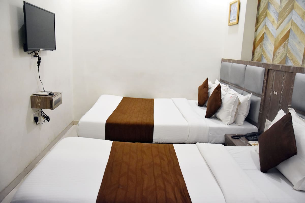 Quarto de hotel com duas camas, uma televisão fixada na parede e cabeceira de madeira.