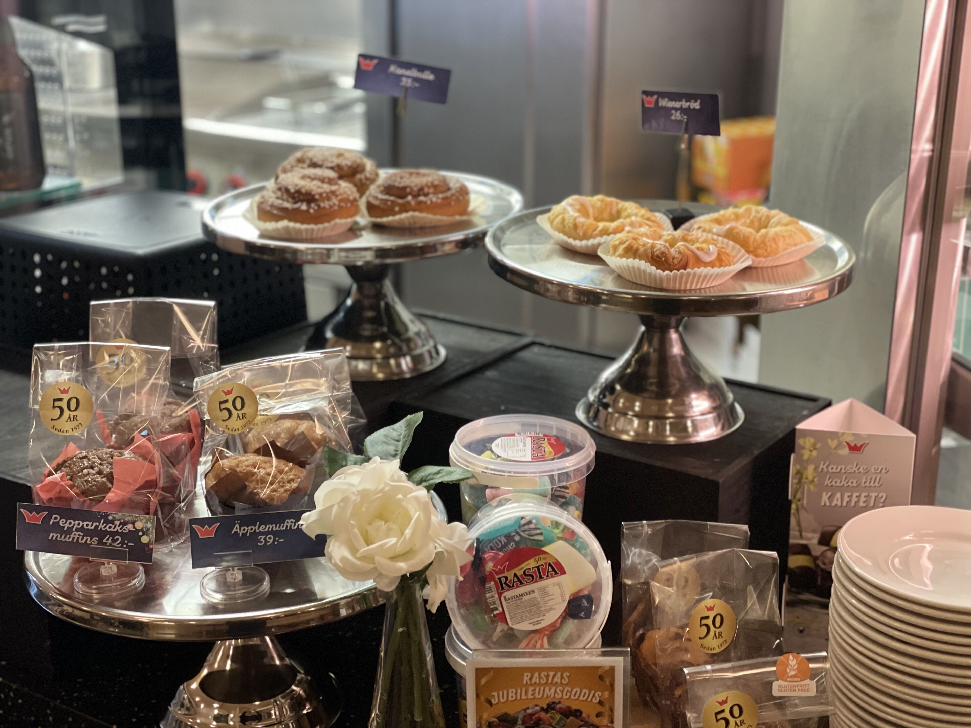 Exposição de doces e produtos de panificação, com etiquetas de preços e indicações de opções sem glúten.
