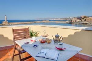 Um terraço com uma mesa posta para chá, uma cadeira e vista para o mar e um farol.