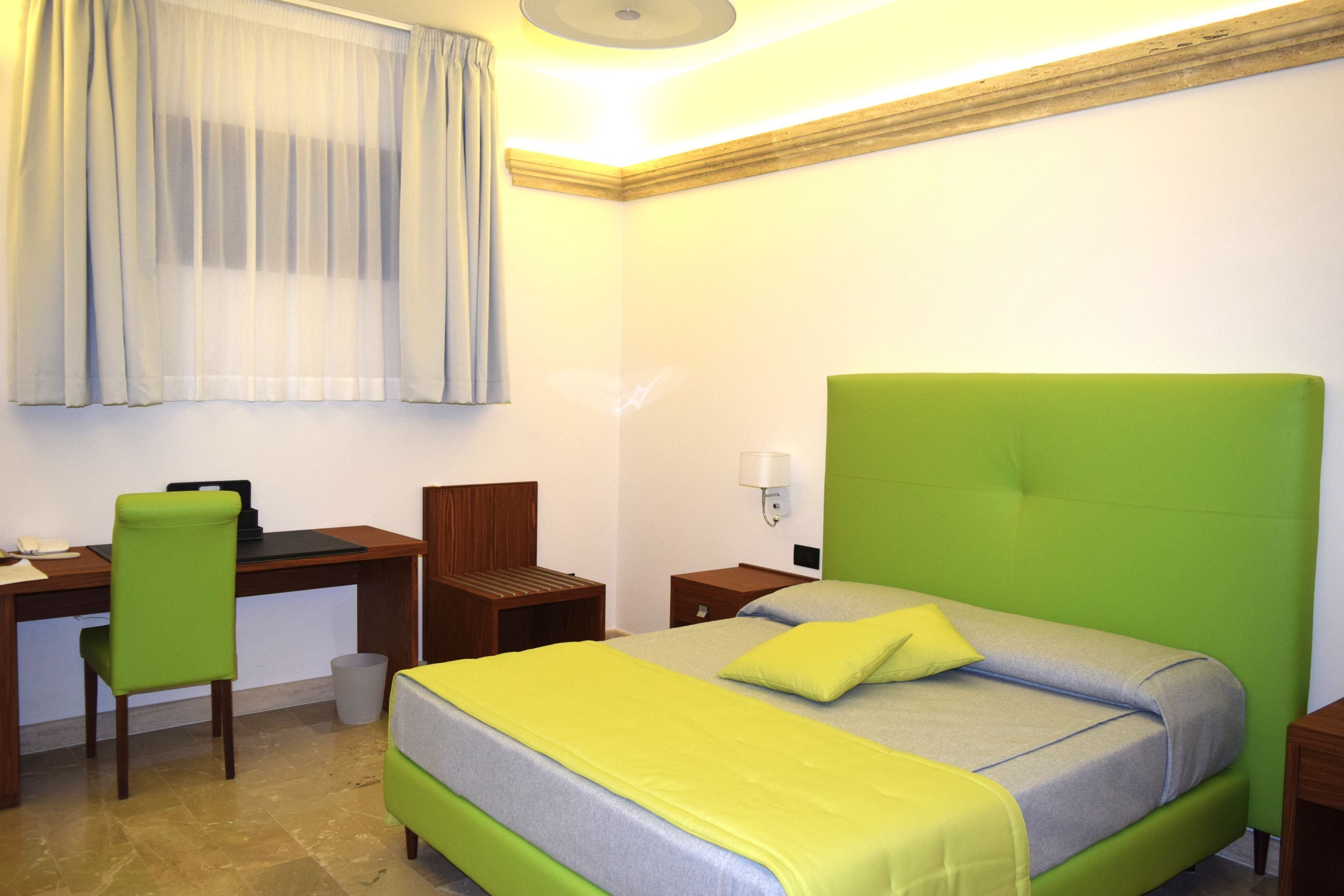Quarto de hotel com cama, escrivaninha, cadeira e luminária.
