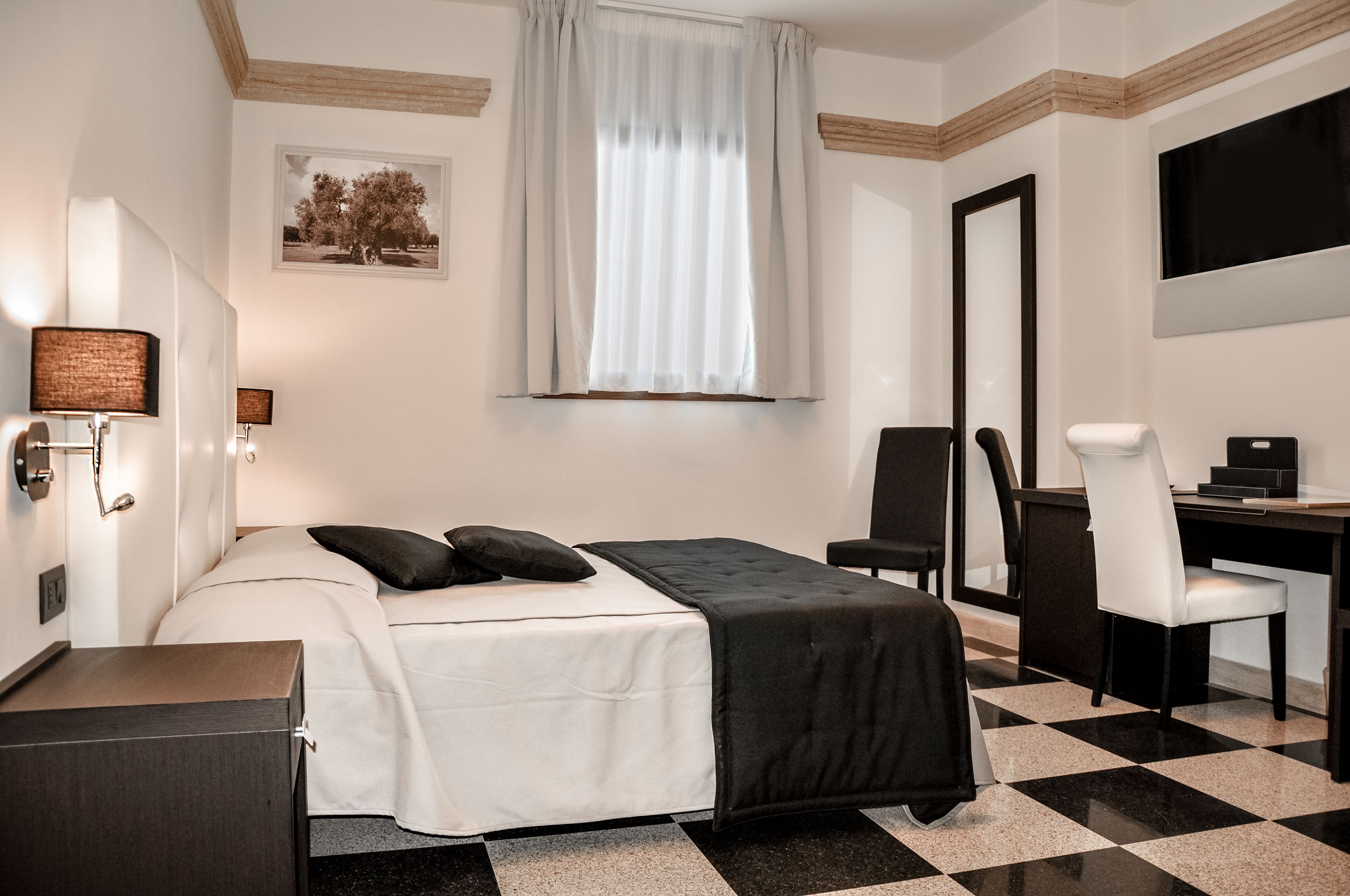 Quarto de hotel com cama, escrivaninha, cadeira, espelho e janela com cortinas.