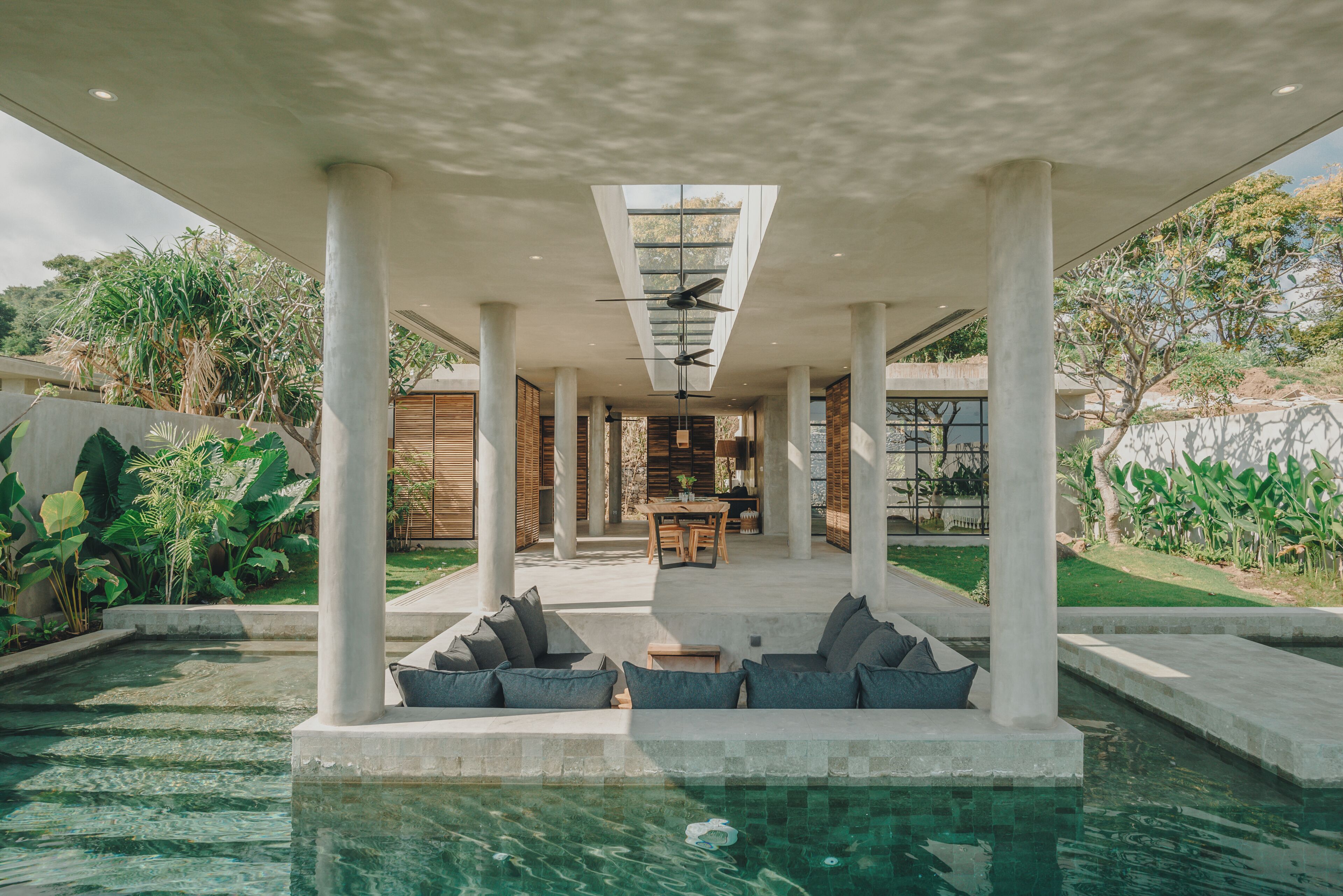 Uma área de piscina moderna ao ar livre, com um espaço de estar coberto, rodeada por vegetação exuberante.