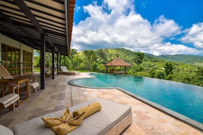 Área da piscina com espreguiçadeira, toalha e vista para uma paisagem verde exuberante com uma colina ao fundo.