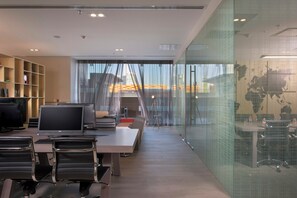 Um espaço de escritório moderno com uma mesa grande, cadeiras, um computador e uma estante de livros.
