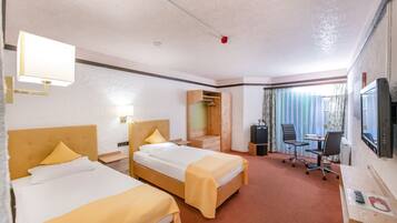 Quarto de hotel com duas camas, uma escrivaninha, uma cadeira, televisão e guarda-roupa.