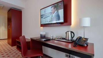 Quarto de hotel com escrivaninha, cadeira, televisão na parede, telefone e cafeteira.