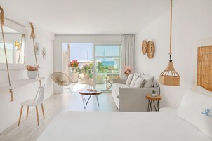 Uma sala de estar clara e moderna, com sofá, poltronas, uma mesinha e vista para o mar através de grandes janelas.