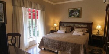 Quarto com uma cama grande, duas mesas de cabeceira com luminárias, uma janela com cortinas e um quadro na parede.