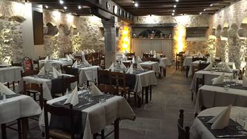 Um restaurante com paredes de pedra, vigas de madeira e mesas postas com toalhas e guardanapos brancos.