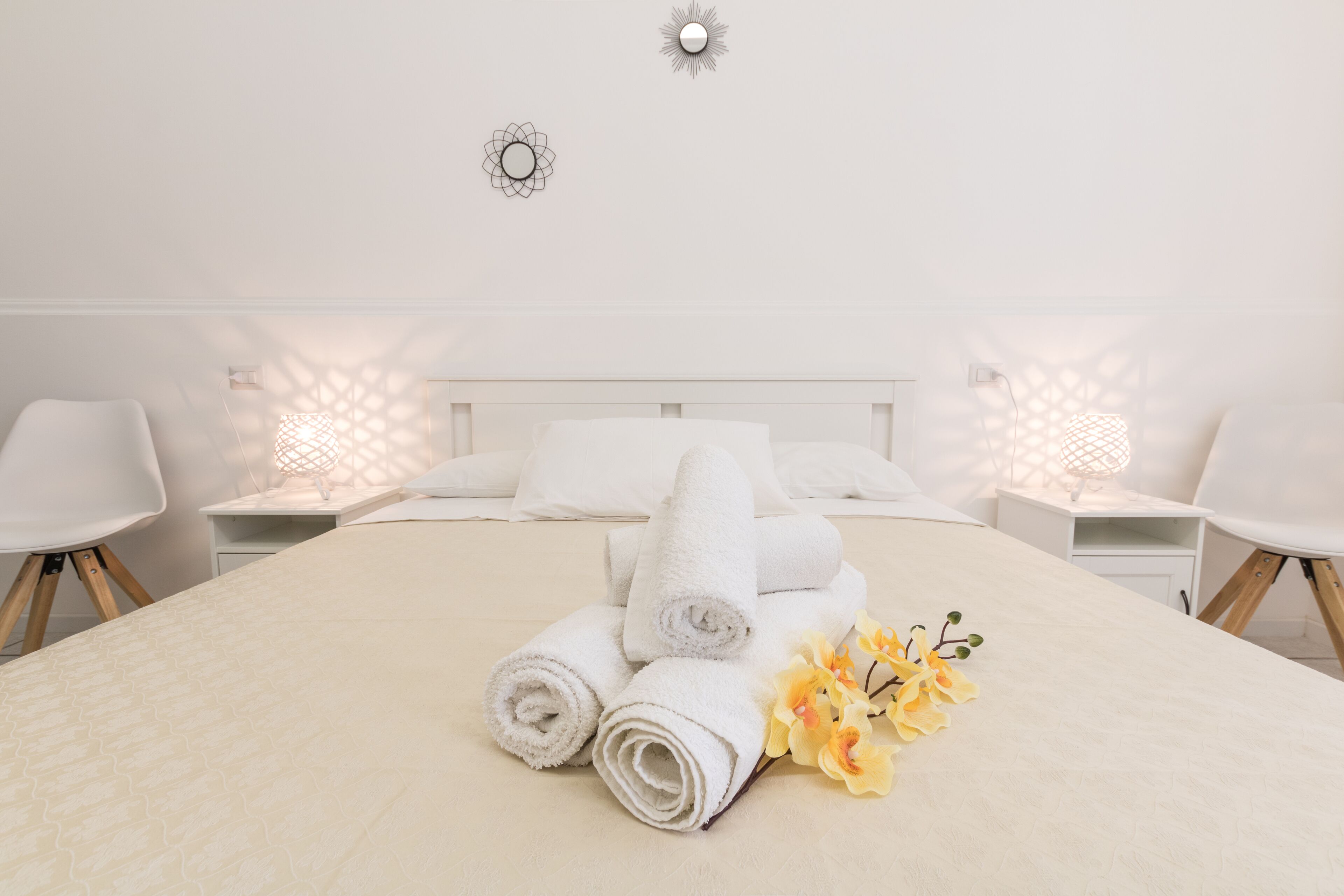 Cama bem arrumada com toalhas brancas dobradas e um vaso de flores amarelas.