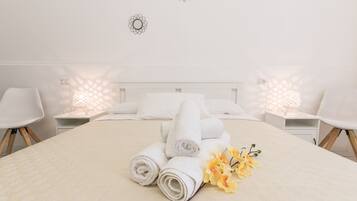 Cama bem arrumada com toalhas brancas dobradas e um vaso de flores amarelas.